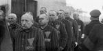 Prisoners wearing pink triangles on their uniforms are marched outdoors ...